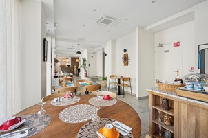 Uma área de refeições moderna com uma mesa de madeira posta para quatro pessoas, rodeada por cadeiras. Há uma cozinha com bancada e diversos utensílios.