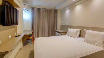Quarto de hotel com cama, escrivaninha, cadeira, televisão e aparelho de ar condicionado.