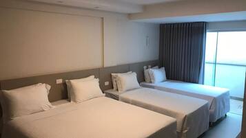 Quarto de hotel com duas camas de solteiro, uma janela grande com cortinas e uma paleta de cores neutras.