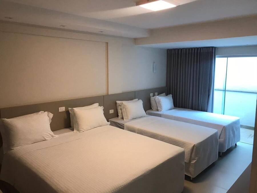 Quarto de hotel com duas camas de solteiro, uma janela grande com cortinas e uma paleta de cores neutras.