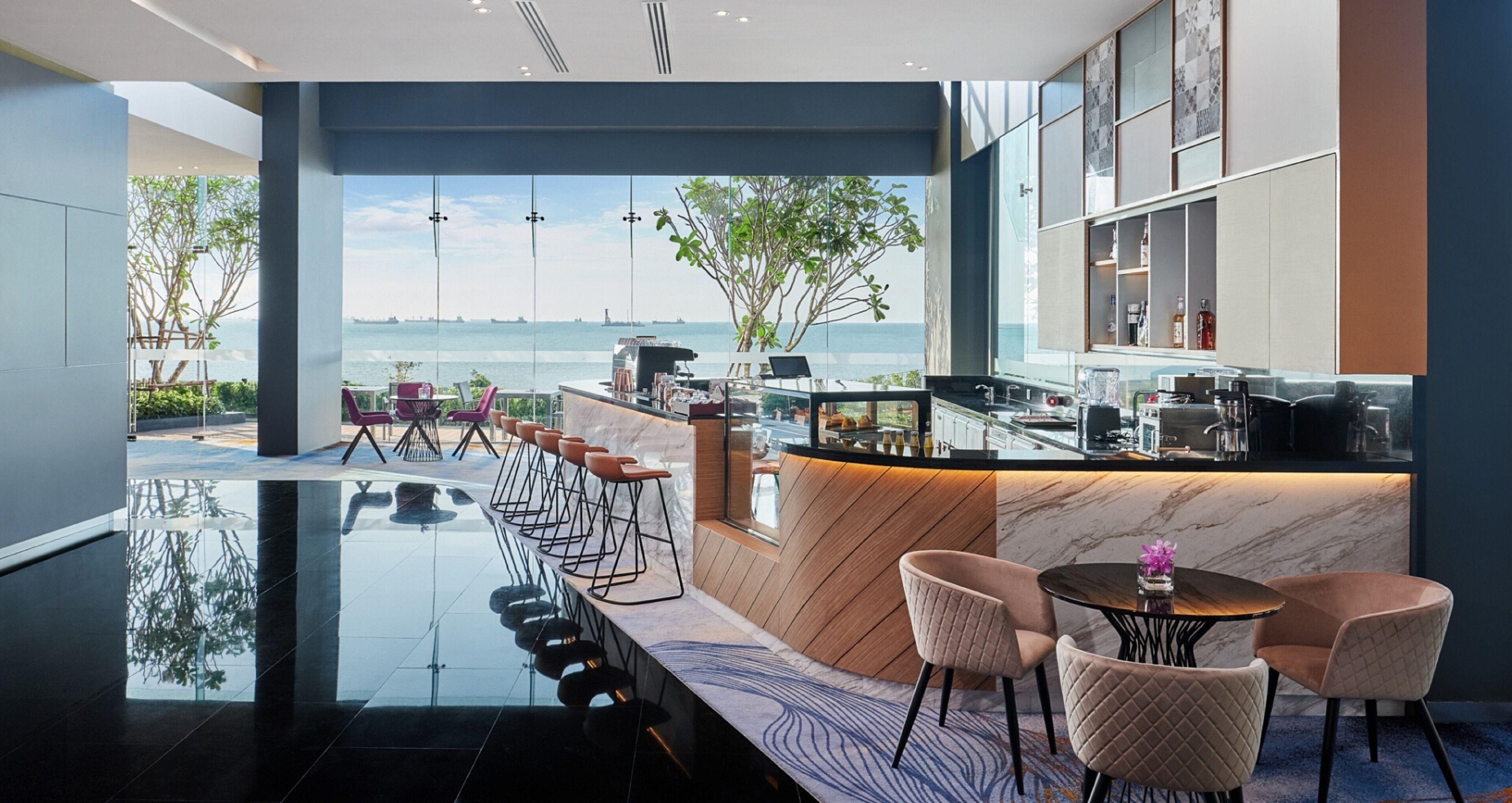Uma área de bar moderna com um balcão comprido, banquetas e vista para o mar.