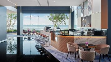 Uma área de bar moderna com um balcão comprido, banquetas e vista para o mar.