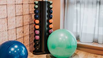 Espaço fitness com equipamentos de exercício, uma bola de exercício azul e uma verde, e piso de madeira.