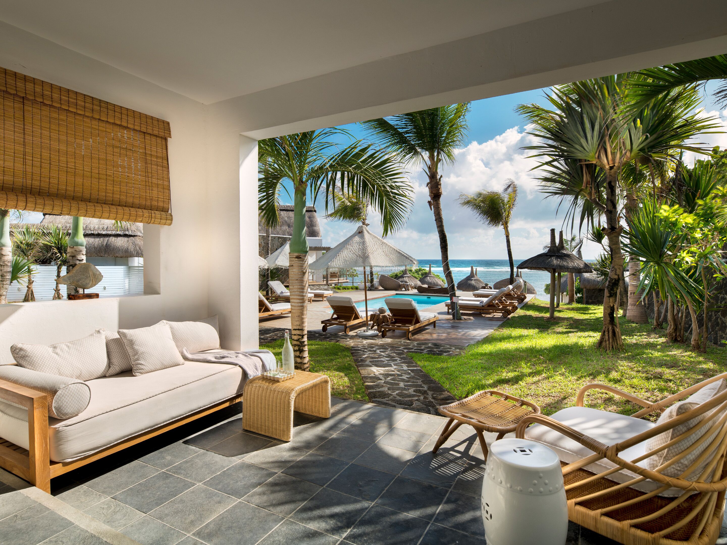 Uma área de estar moderna ao ar livre, com um sofá, cadeiras de vime e vista para a piscina.