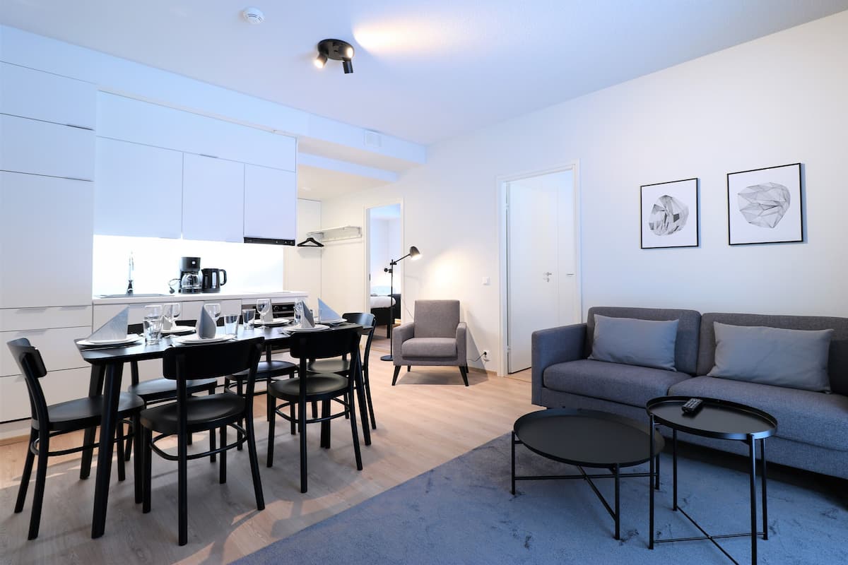 Uma sala de estar moderna com um sofá cinzento, uma mesa de centro e uma área de jantar com uma mesa posta para quatro pessoas.