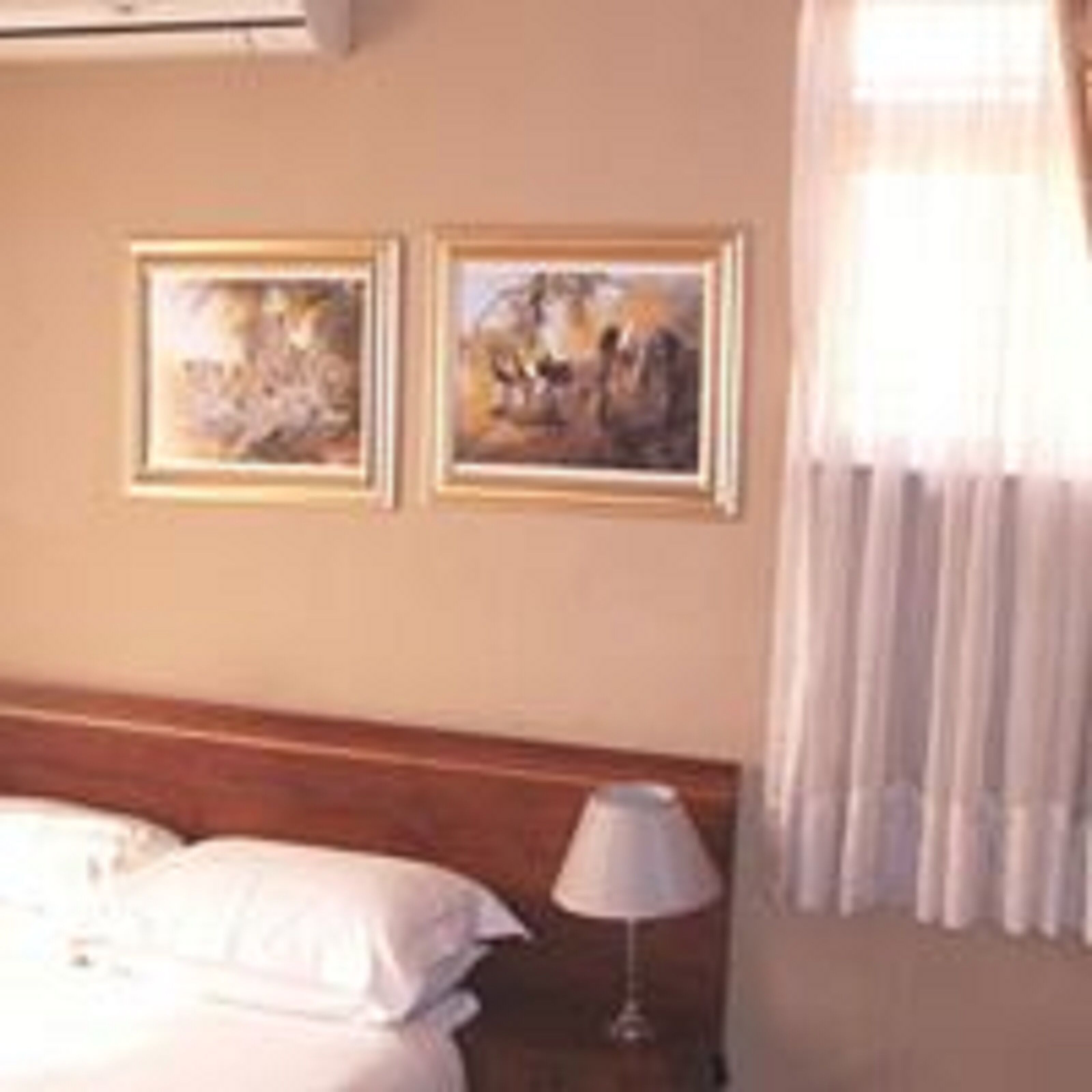 Quarto de hotel com cama, mesa de cabeceira, luminária e duas imagens emolduradas na parede.