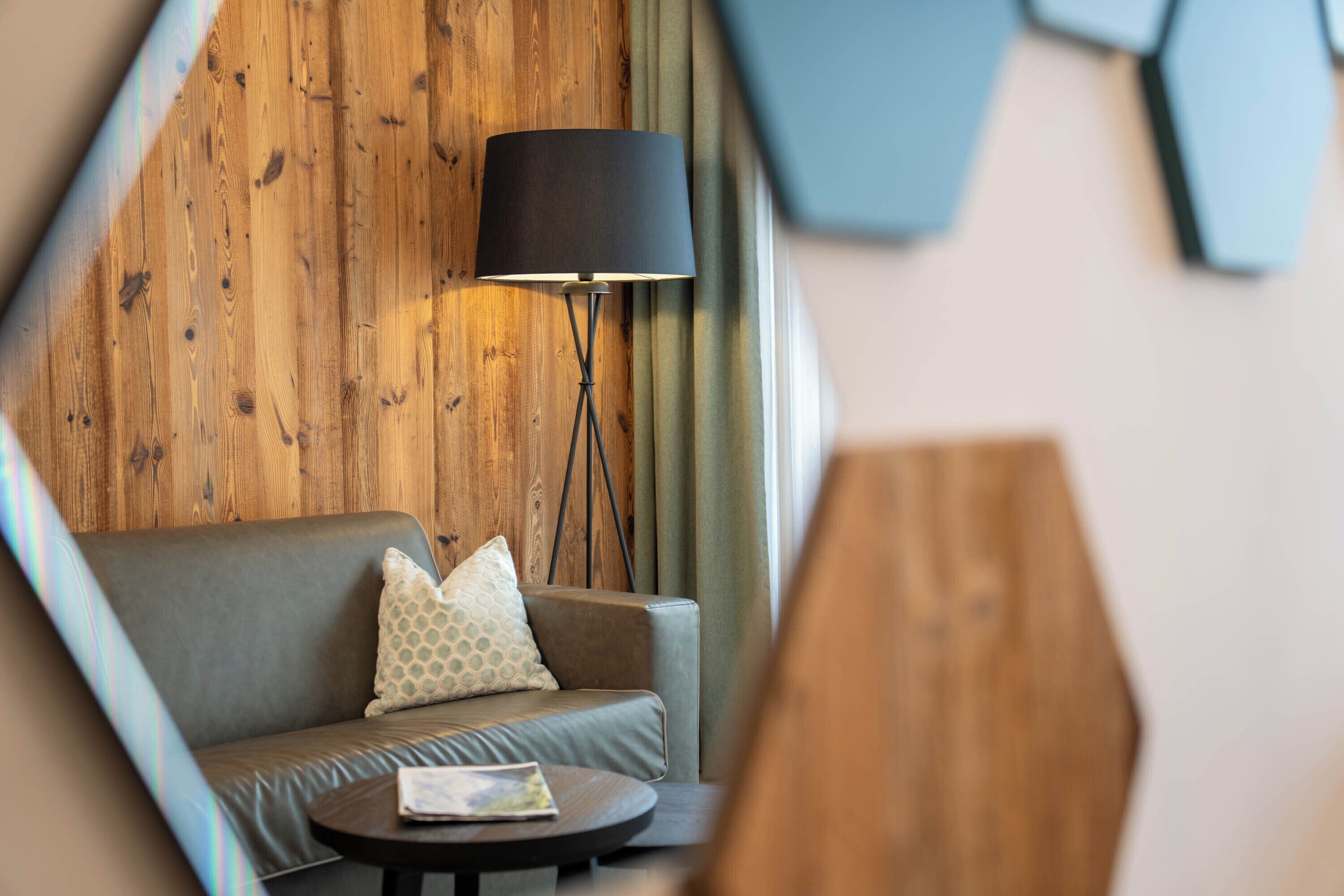 Um interior moderno com uma parede de madeira, um sofá cinza com almofadas estampadas, um abajur de chão preto e uma pequena mesa redonda com uma revista.