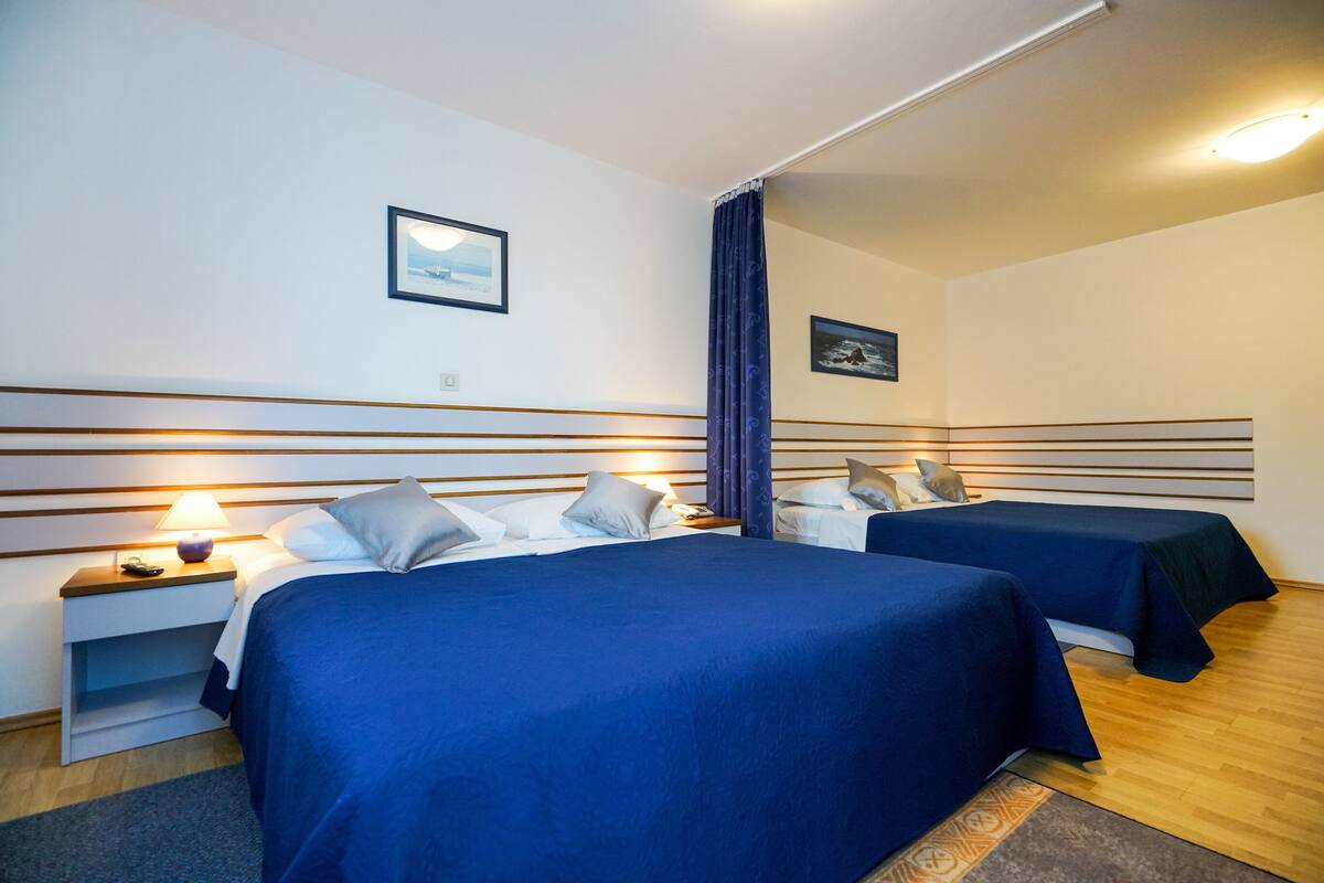 Quarto de hotel com duas camas, uma mesa de cabeceira com abajur e um quadro na parede.
