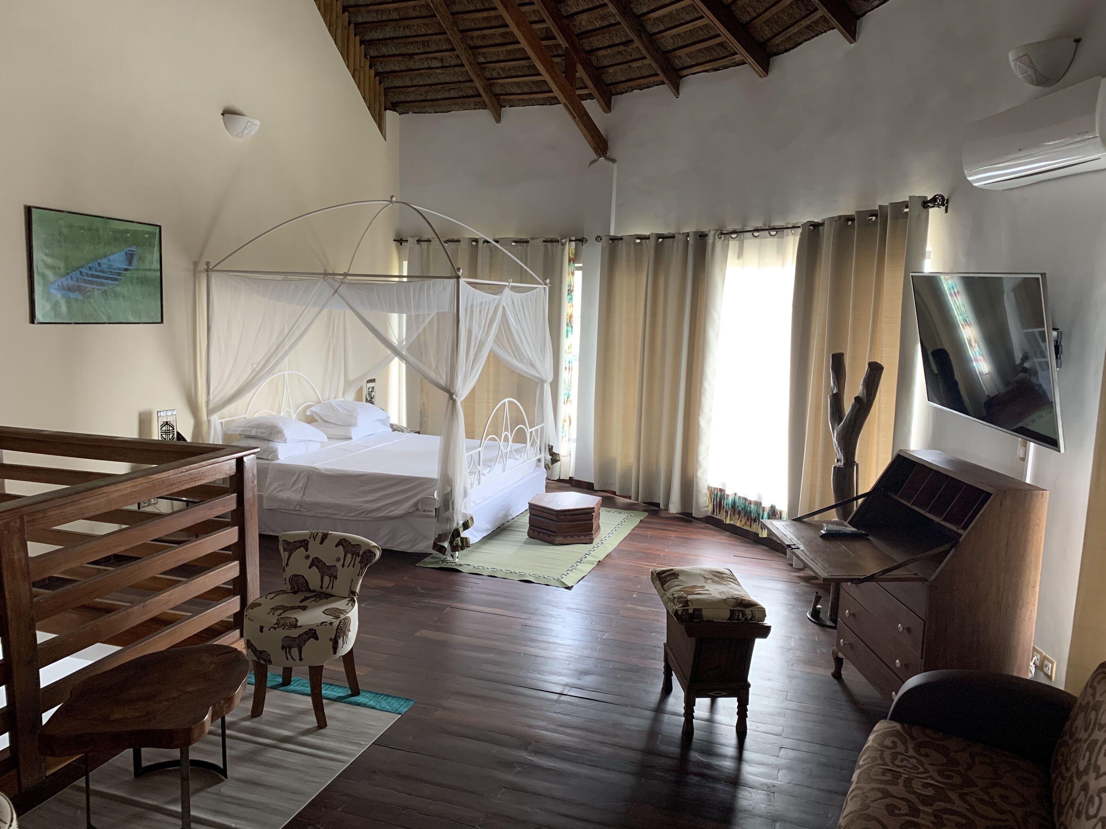 Quarto com cama de dossel, televisão, escrivaninha de madeira e uma cadeira.