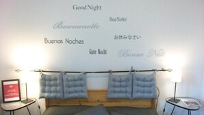 Quarto de hotel com uma cama, mesas de cabeceira e uma parede com placas em vários idiomas que dizem 'Boa Noite'.