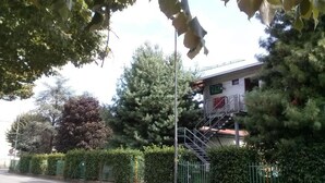Um edifício com escadaria que dá para um varanda, cercado por vegetação e uma grade.