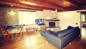 Uma sala de estar acolhedora com parede de pedra, piso de madeira, lareira, televisão e sofá azul.