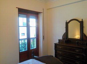 Um quarto com cômoda de madeira, cama com colcha branca e um espelho grande.