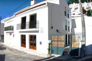 Um edifício branco de dois andares com varanda, portão e placa de proibido estacionar.