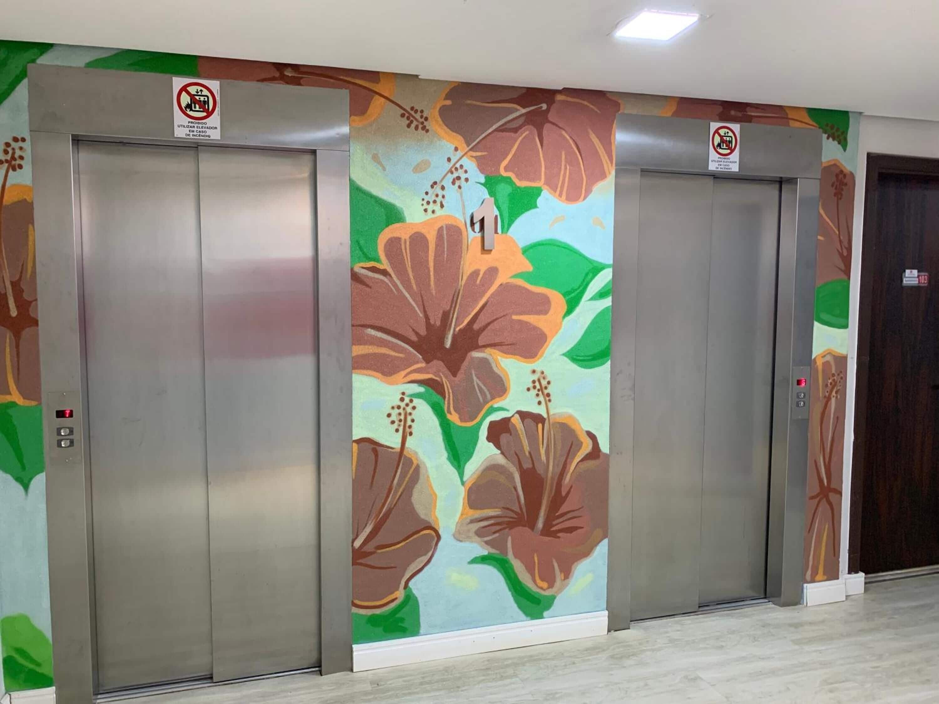 Dois elevadores com arte floral nas paredes e um aviso de proibido fumar.