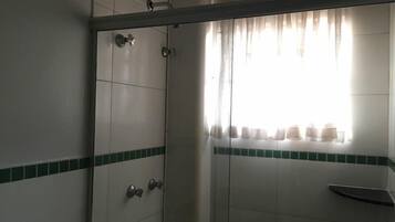 Casa de banho com chuveiro, paredes em azulejo e janela com cortinas.