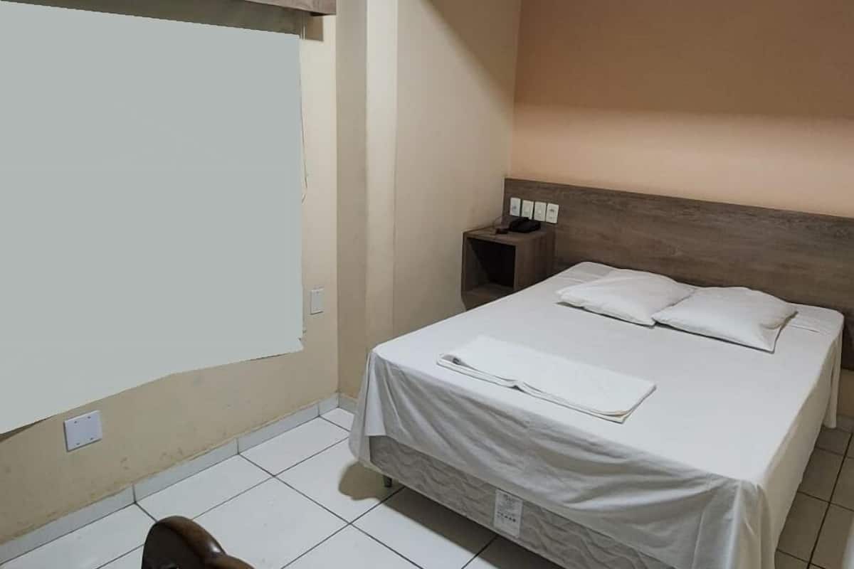 Quarto pequeno e limpo, com uma cama, mesa de cabeceira e uma cadeira.