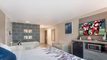 Quarto de hotel com cama, televisão, secretária com micro-ondas e casa de banho com banheira.