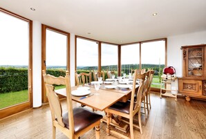 Uma sala de jantar com uma mesa grande posta para seis pessoas, cadeiras de madeira e vista para o exterior.