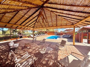 Uma área externa coberta com espreguiçadeiras, piscina e vista para a paisagem ao redor.