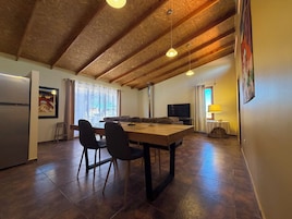 Uma área de refeições com mesa e cadeiras de madeira, televisão e um quadro na parede.
