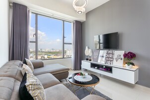 Uma sala de estar moderna com uma janela grande, um sofá, uma mesa de centro e uma TV sobre um móvel branco.