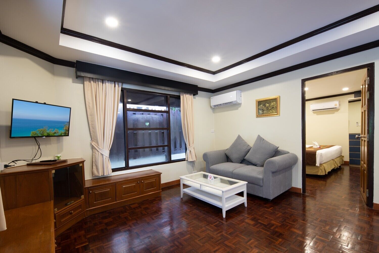 Uma sala de estar com sofá, mesa de centro, televisão e janela com cortinas.