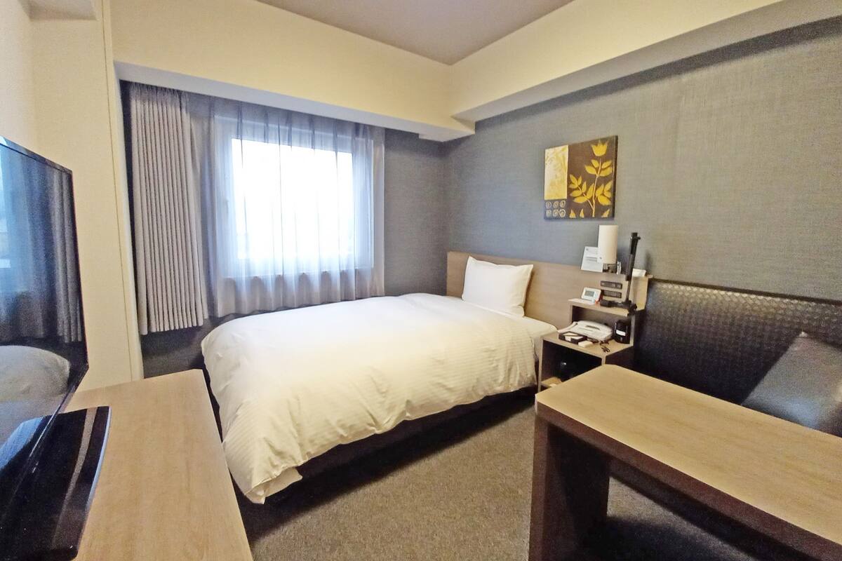 Quarto de hotel com cama, mesa de cabeceira e pequena escrivaninha.