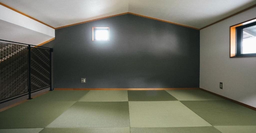 Quarto com piso de esteira de tatame, parede escura, janela pequena e teto de madeira.
