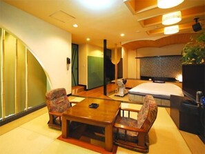 Quarto de hotel com uma cama, televisão, escrivaninha e duas cadeiras.