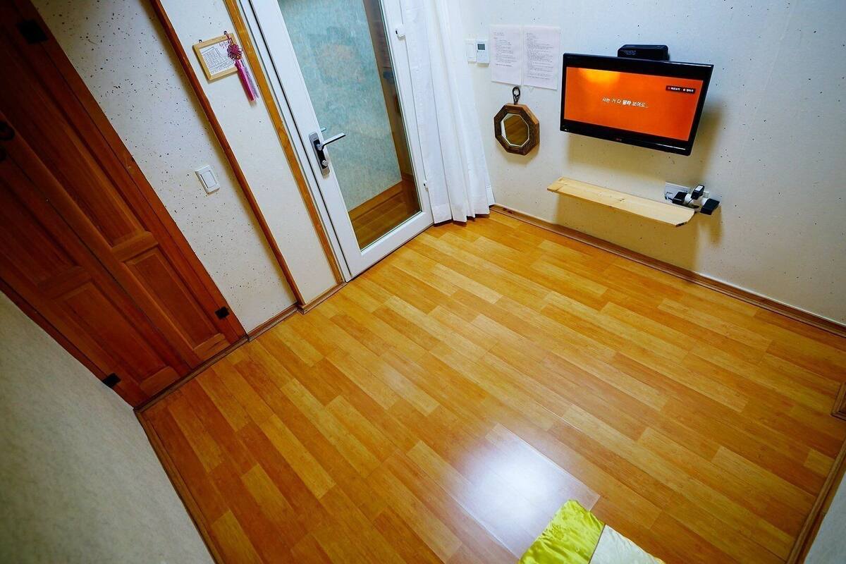 Quarto com piso de madeira, porta deslizante, televisão montada e uma pequena prateleira.