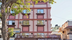 Um hotel de vários andares com uma varanda no segundo andar, uma placa com 'Hotel Riverfront' e uma árvore ao primeiro plano.