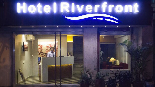 Hotel à beira do rio, com balcão de recepção, um recepcionista e plantas em vasos do lado de fora.