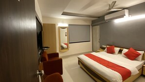 Quarto de hotel com cama, televisão, espelho, porta e ventoinha no teto.