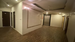 Um corredor com piso de madeira, uma parede branca e uma porta com a inscrição '105', além de um elevador.