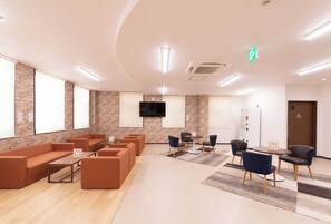 Um hall amplo com área de estar, uma TV de tela plana na parede e um balcão de recepção.