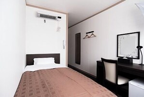Quarto de hotel com cama, escrivaninha, cadeira, espelho e ar condicionado.