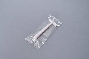Embalagem de plástico transparente com um objeto branco no interior, sobre uma superfície cinzenta.