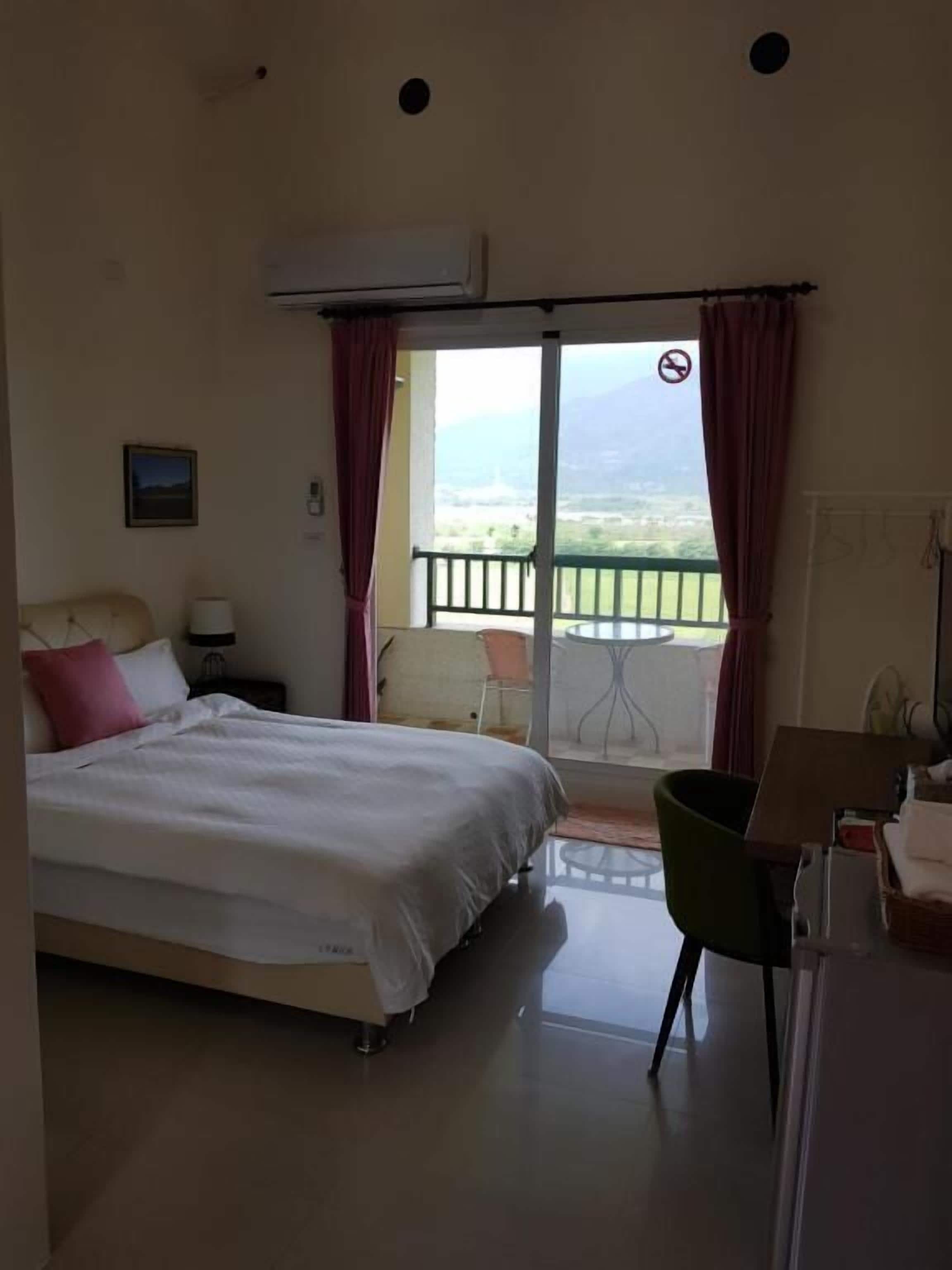 Quarto de hotel com cama, escrivaninha, cadeira, varanda com vista e ar condicionado.
