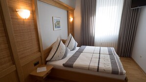 Uma cama bem arrumada com almofadas e um cobertor, uma mesa de cabeceira com abajur e uma janela com cortinas.