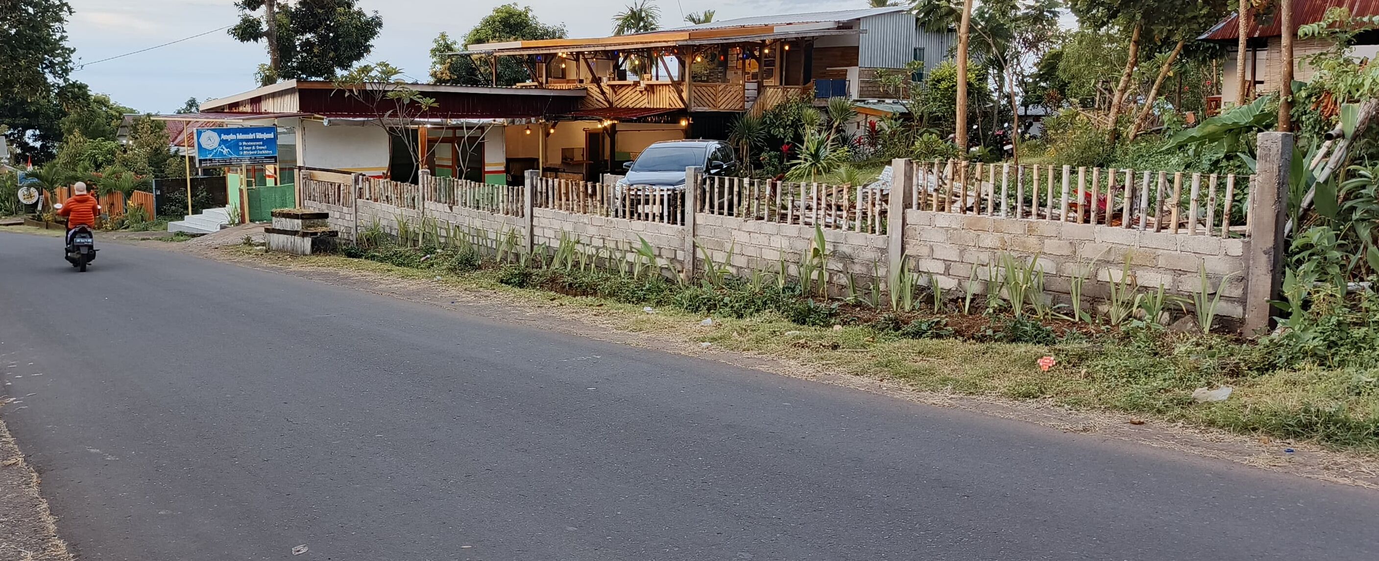 Um edifício com uma placa, um carro estacionado em frente e uma motocicleta com o condutor.