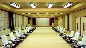Uma sala de conferências com fileiras de cadeiras brancas, uma mesa comprida e piso coberto de carpete.