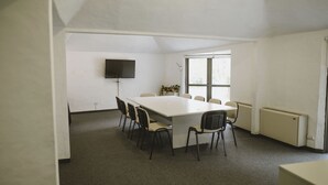 Uma sala de conferência com uma grande mesa, cadeiras, uma TV de tela plana e uma janela com persianas.