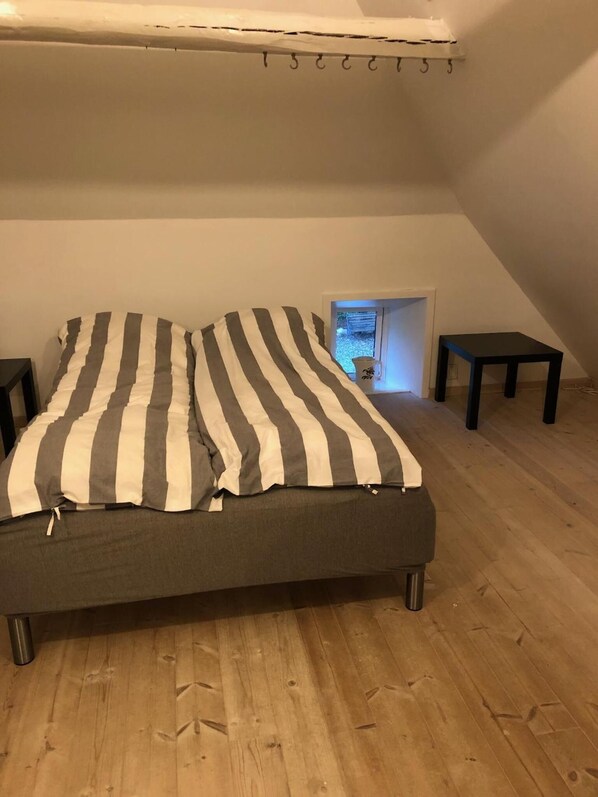 Um quarto de sótão pequeno e acolhedor, com cama, uma mesinha e uma janela.