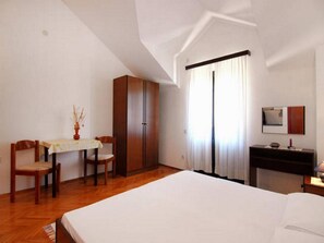 Quarto com cama, guarda-roupa de madeira, secretária com cadeira e janela com cortinas.