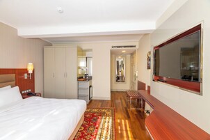 Quarto de hotel com cama, escrivaninha, televisão e banheiro visível por uma porta aberta.