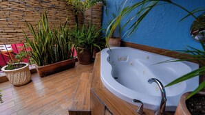 Uma área de spa com uma banheira grande, piso de madeira e diversos vasos com plantas.