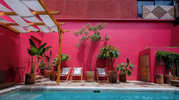 Uma área de piscina com parede vermelha, espreguiçadeiras e plantas em vasos.