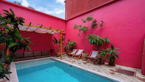 Piscina com parede vermelha, espreguiçadeiras e plantas em vasos.