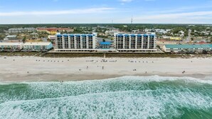 Um hotel à beira-mar com vários andares, uma praia de areia em frente e ondas quebrando na costa.